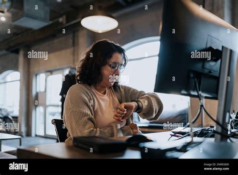 Female Computer Programmer Checking Time On Wristwatch While Working At