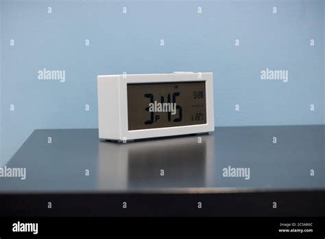 Selective Focus Shot Of A Digital Clock Showing The Time On A Table By A Blue Wall Stock Photo