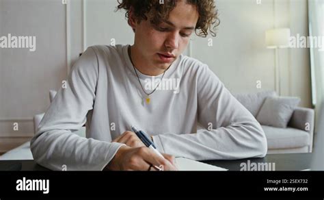 Handsome Man Makes Notes In A Notebook While Sitting In Front Of Open Laptop Stock Video Footage