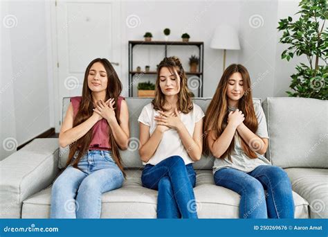 Group Of Three Hispanic Girls Sitting On The Sofa At Home Smiling With