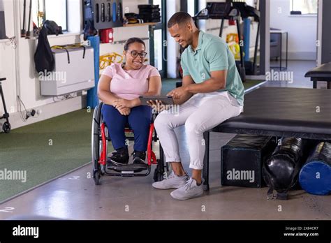 Biracial Male Therapist Showing Tablet To A Female Paraplegic Patient