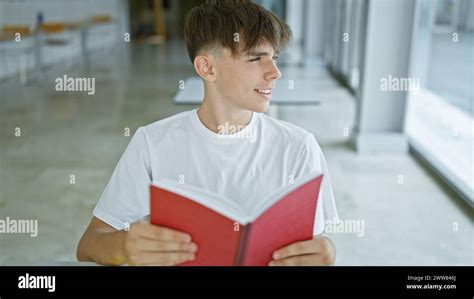 A Cheerful Young Man With Blond Hair Sits Reading In A Casual College
