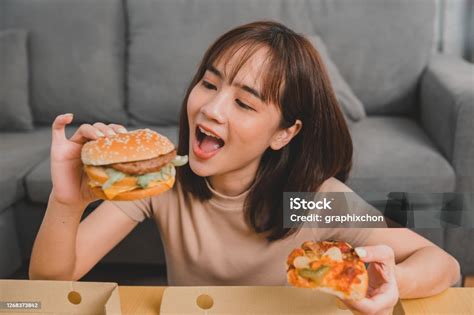 패스트 푸드 테이크 아웃 집으로 돌아갑니다 테이크 아웃 및 배달 시 햄버거를 먹는다 거실에서 아시아 여성의 라이프 스타일 사회적 불변과 새로운 정상 먹기에 대한 스톡 사진