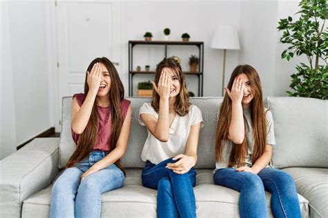 Group Of Three Hispanic Girls Sitting On The Sofa At Home Covering One