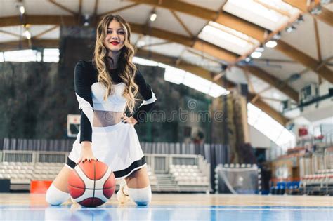 Nice Looking Pretty Cheerleader In Black White Uniform Posing With A Ball In The Arena Stock