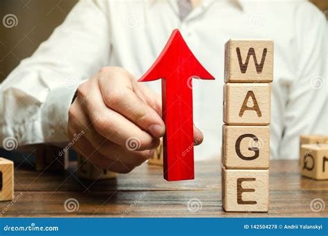 Businessman`s Hand Holds Red Arrow Up Near Wooden Blocks With Word Wage