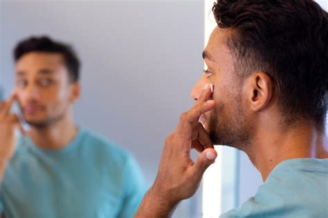 Premium Photo | Biracial man looking at himself in bathroom mirror and applying face cream ...