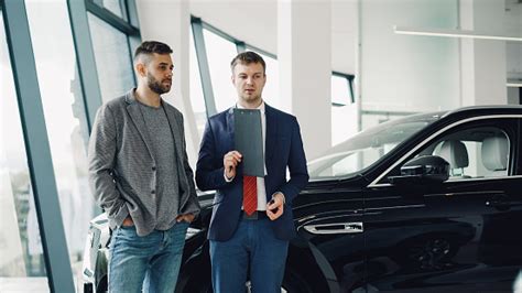 잘생긴 남자는 새로운 자동차 모델을 논의 하는 모터쇼에서 자동차 대리점 관리자 딜러 문서와 펜을 들고 있다 구매 차량 및 사람들 개념입니다 차에 대한 스톡 사진 및 기타