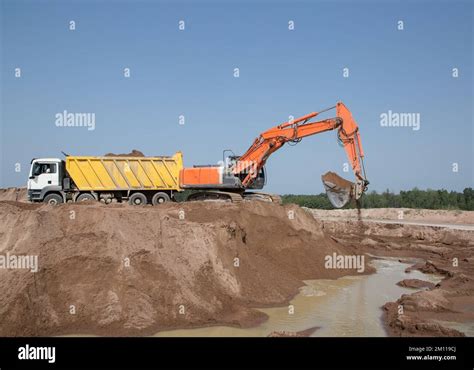 Large Bucket Of An Orange Crawler Excavator Pours Earth Into A Yellow