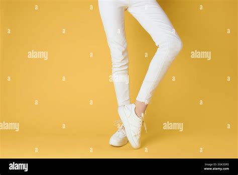 Female Legs In White Pants Sneakers Fashion Yellow Background Stock