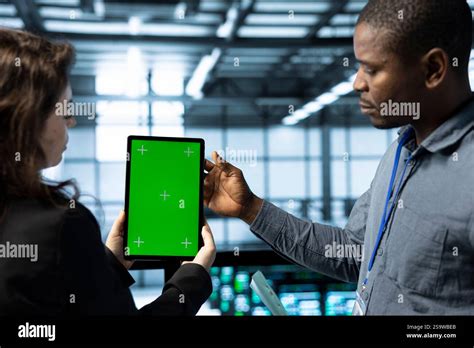 Engineers In Data Center Using Mockup Tablet Observing Analytics Reviewing Supercomputer Gear