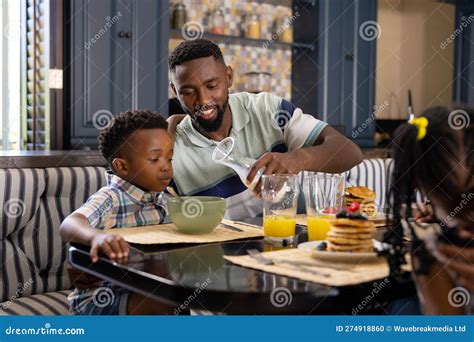 African American Father Pouring Milk in Bowl for Son while Having Breakfast at Dining Table ...