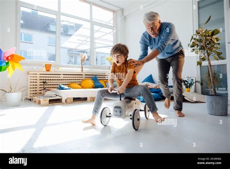 Cheerful Grandfather Pushing Grandson Sitting On Toy Car In Living Room Stock Photo Alamy