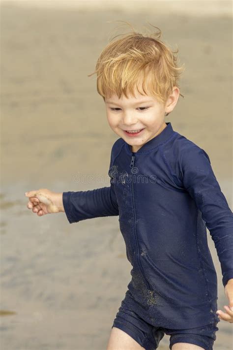 Young Boy With Blonde Hair And Navy Swimsuit Having Fun Splashing At