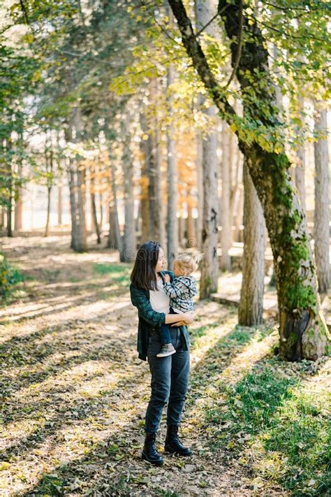 Mom With A Little Daughter In Her Arms Stands In The Forest And Looks