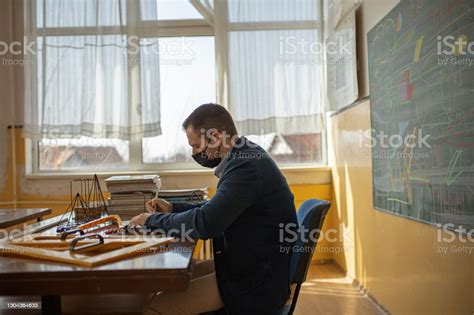 Side View Of Teacher Sitting At School Desk Behind The Window Stock