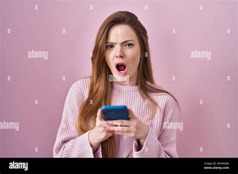 Young Caucasian Woman Using Smartphone Typing Message Angry And Mad