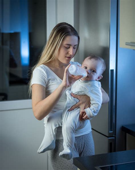 Madre Joven Que Da La Leche Del Hijo Del Bebé De La Botella En Cocina