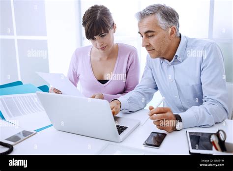Executive Working At Office Desk With His Young Assistant They Are