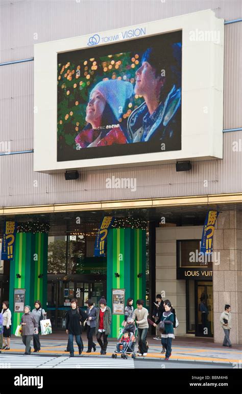 Pedestrians Wait At Crosswalk Beneath Large Lcd Screen Above Entrance