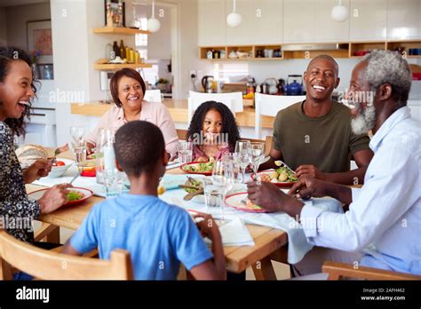 Multi-Generation Family Sitting Around Table At Home Enjoying Meal Together Stock Photo - Alamy