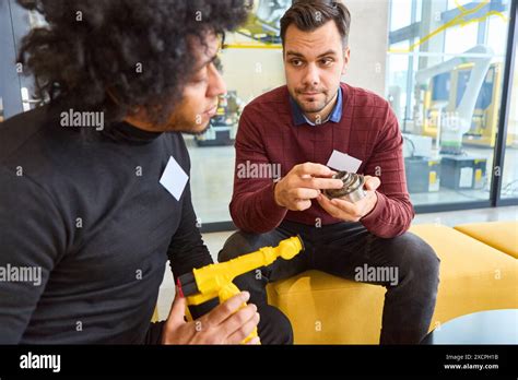 Two Engineers Examining And Discussing Parts Of A Robotic Arm In An