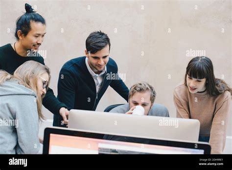 Male Computer Programmer Drinking Coffee While Using Computer With Colleagues In Office Stock