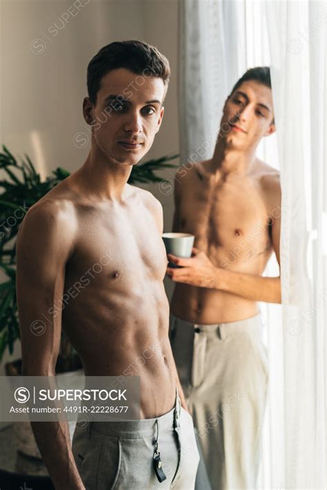 Stylish Shirtless Gay Couple Posing In Front Of The Camera Standing Near Windows Drinking Coffee