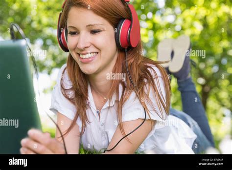 Pretty Redhead Using Her Tablet Pc While Listening To Music In The Park