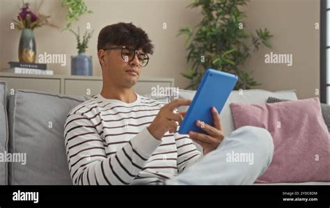 Attractive Young Hispanic Man In Glasses Using A Blue Tablet While