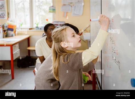 Blond Girl Solving Maths Problem While Writing On Whiteboard In