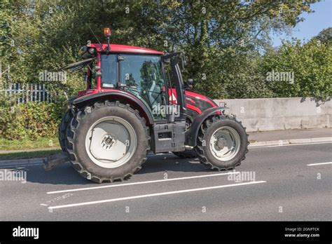 Side Profile Of Red Valtra Farm Tractor On Open Uphill Rural Country