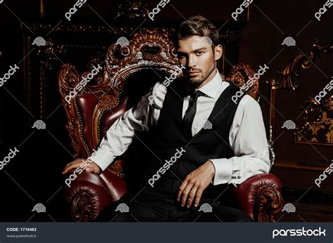 مرد باشکوه با لباسی که روی صندلی راحتی در آپارتمانی مجلل با فضای داخلی کلاسیک نشسته است لوکس