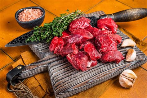 Raw Beef Meat Chopped In Cubes On Wooden Cutting Board For Cooking Stew Orange Background Stock