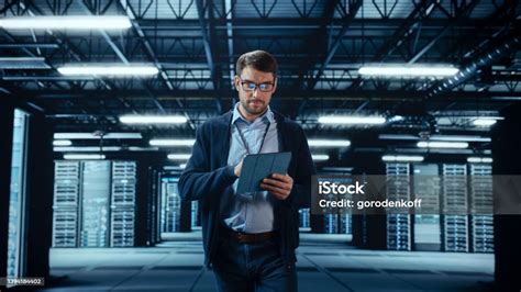 남성 It 전문가가 데이터 센터의 운영 서버 랙 행 사이를 안내합니다 엔지니어는 유지 보수를 위해 태블릿 컴퓨터를 사용합니다