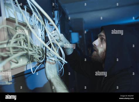 Concentrated Young Bearded Hacker In Hoodie Checking Cables Of Network Server And Breaking
