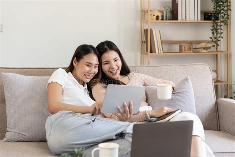 Happy Two Young Asian Girls Are Sitting On Couch Using Digital Tablet