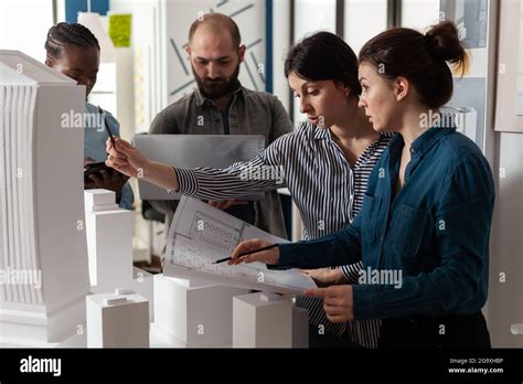 Team Of Diverse Architects Discussing Blueprint Plans On Paper Laptop Computer Tablet