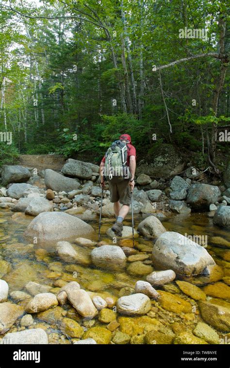 A Hiker Crossing The Swift River Along The Sawyer River Trail In The