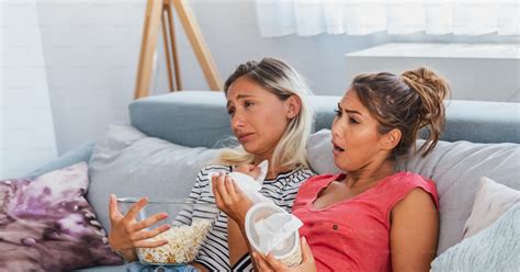 두 명의 가장 친한 친구가 침대에서 슬픈 영화를 보고 만지고 울고 있다 소녀들은 팝콘과 Tv 리모컨을 들고 텔레비전에서 화면 로맨틱 영화를 봅니다 파자마를 입은 숙녀들이