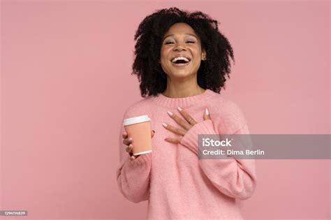 곱슬 머리를 가진 쾌활한 어두운 피부 밀레니엄 여성은 뜨거운 커피 또는 차 테이크 아웃의 종이 컵을 들고 카메라를보고 핑크