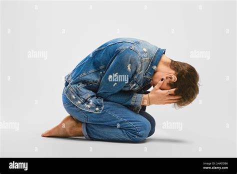 Desperate Young Man Kneels On The Floor And Covers Face With Hands