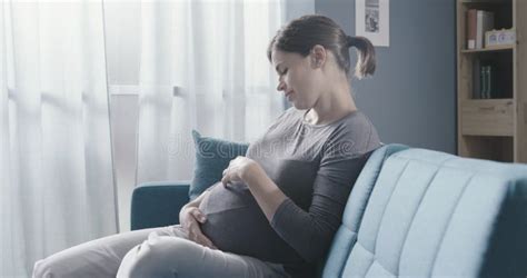Happy Pregnant Woman Stroking Big Belly with Love and Showing Thumbs Up Sign Sitting on Home ...