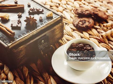 고리버들 배경에 커피 원두와 초콜릿 칩 쿠키가 있는 흰색 컵 설탕 초콜릿 달콤한 스틱 및 계피 조각의 나무 상자에 0명에 대한