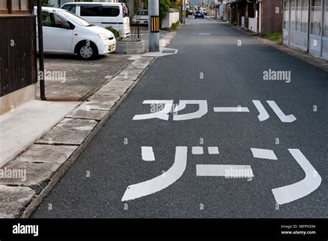 Japanese Katakana Script Written On The Roadway Warns Drivers Of A School Zone And To Alert