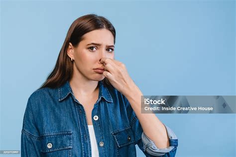 Young Woman Plugging Nose On Blue Background For Funny Concept Stock