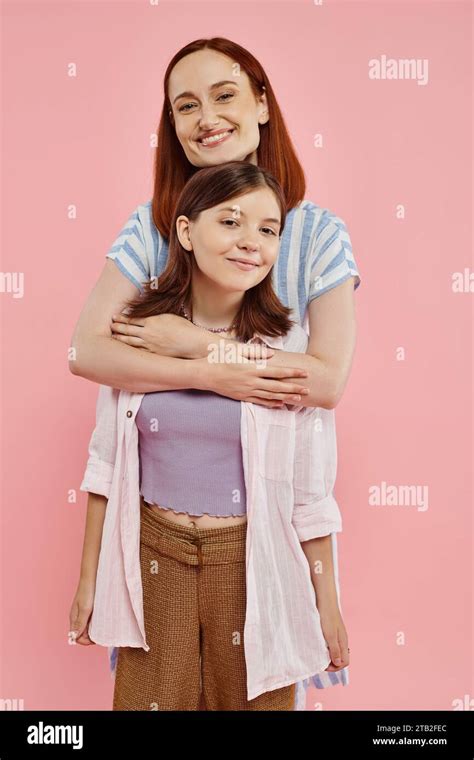 Cheerful And Stylish Woman Hugging Smiling Preteen Daughter On Pink