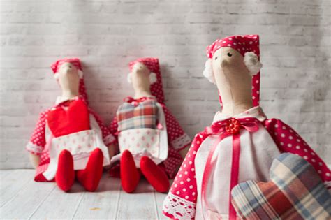 빨간 드레스를 입은 세 개의 물결인형과 흰 앞치마 그리고 붉은 칼팍이 밝은 배경에 앉아 있다 인테리어 인형입니다 텍스트에 대한 장소가 있습니다 바느질의 개념 갈색에 대한