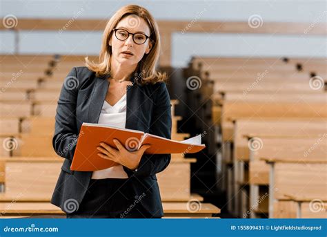 Female University Professor Holding Journal And Looking At Camera Stock