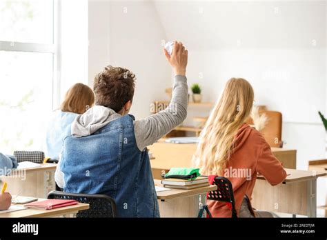 Male Student Throwing Crumpled Paper In His Classmates At Classroom